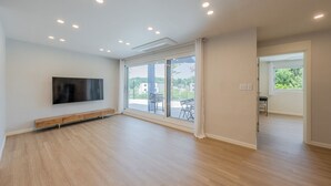 Um quarto espaçoso com televisão de tela plana, piso de madeira, janelas amplas e uma porta de vidro deslizante para área externa.