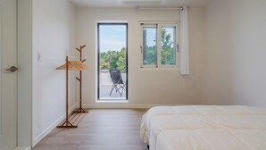 Quarto com cama, varal de madeira, janela e varanda com cadeira.