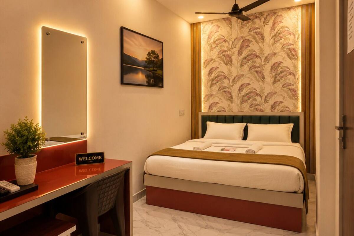 Quarto de hotel com uma cama, uma escrivaninha com a placa 'WELCOME', um ventilador de teto e uma parede com papel de parede floral.