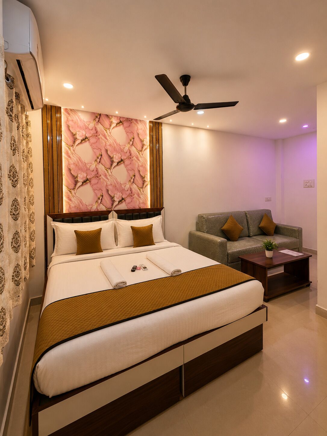 Quarto de hotel moderno com uma cama grande, um sofá, um ventilador de teto e parede com padrão de mármore.