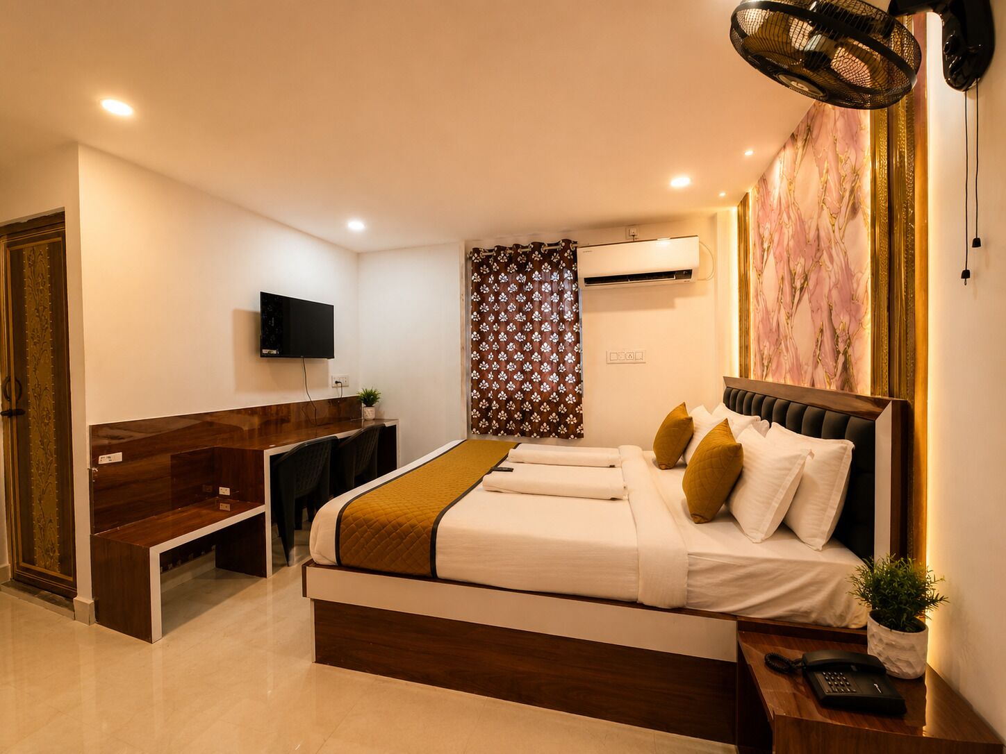 Quarto de hotel moderno com cama, mesa de cabeceira, televisão, aparelho de ar condicionado e um detalhe decorativo na parede.
