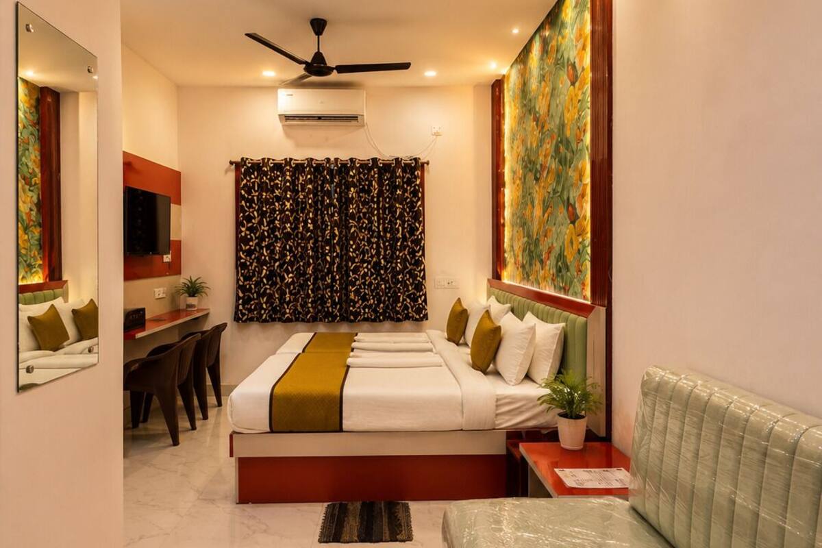 Quarto de hotel com cama, sofá, escrivaninha, cadeira, televisão e ventoinha de teto.