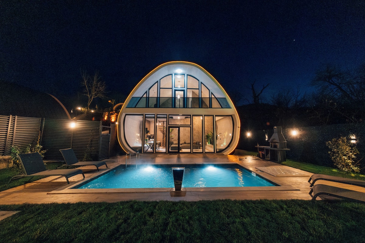 Uma casa moderna com piscina, cadeiras de descanso e uma entrada bem iluminada.