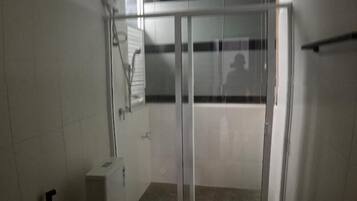 Casa de banho com sanita, chuveiro e porta de vidro que dá para uma varanda.