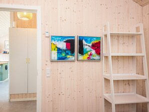 Quarto com paredes de painel de madeira, um guarda-roupa branco, duas pinturas abstratas coloridas e uma estante branca.