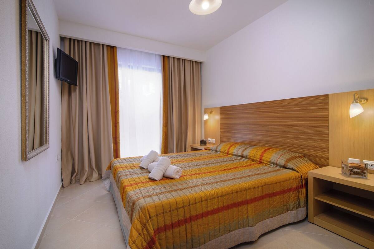 Quarto de hotel com uma cama grande, televisão, mesa de cabeceira e cabeceira.