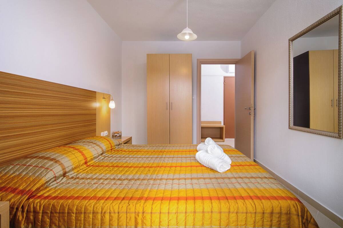 Quarto de hotel com cama, mesa de cabeceira, espelho e guarda-roupa.