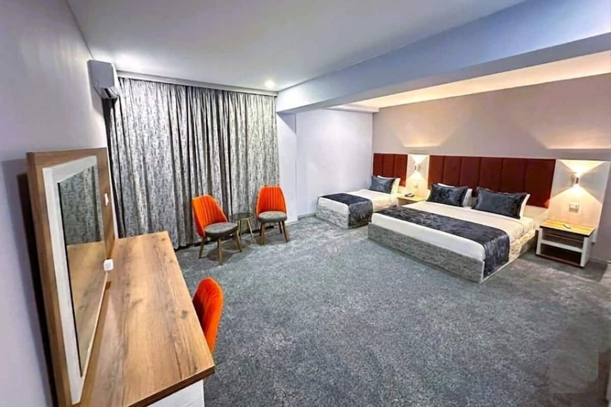 Quarto de hotel com cama, duas cadeiras, uma mesa e uma janela grande com cortinas.