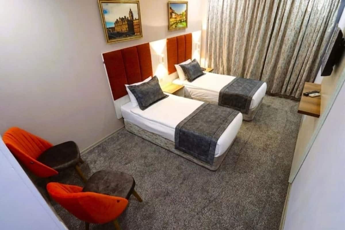 Quarto de hotel com duas camas, um sofá, uma mesinha e uma cadeira.