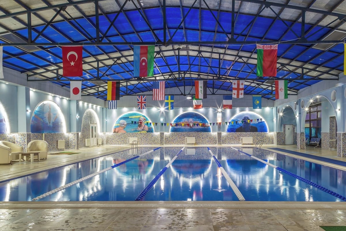 Piscina interna com várias pistas de natação, cercada por arcos e bandeiras de diferentes países.