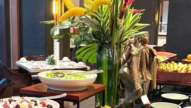 Buffet com diversos pratos, uma planta decorativa e uma placa indicando 'Thai Beef Salad'.