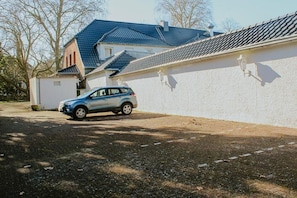 Um edifício branco com telhado azul, um carro estacionado e um caminho de acesso de cascalho.