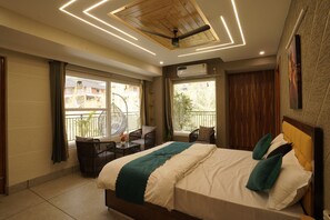 Quarto com cama, ventoinha no teto, janela, varanda e área de estar com mesa e cadeiras.