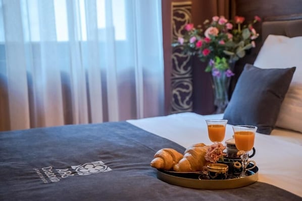 Cama com bandeja de croissants e suco de laranja, um vaso de flores e um espalha cama de cor escura com um logotipo.