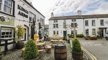 Um pub tradicional com mesas ao ar livre, calçamento de pedra e plantas em vasos.
