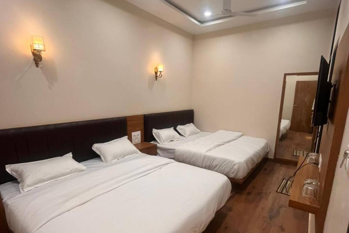 Quarto de hotel com duas camas, ventoinha no teto, iluminação embutida, televisão e piso de madeira.