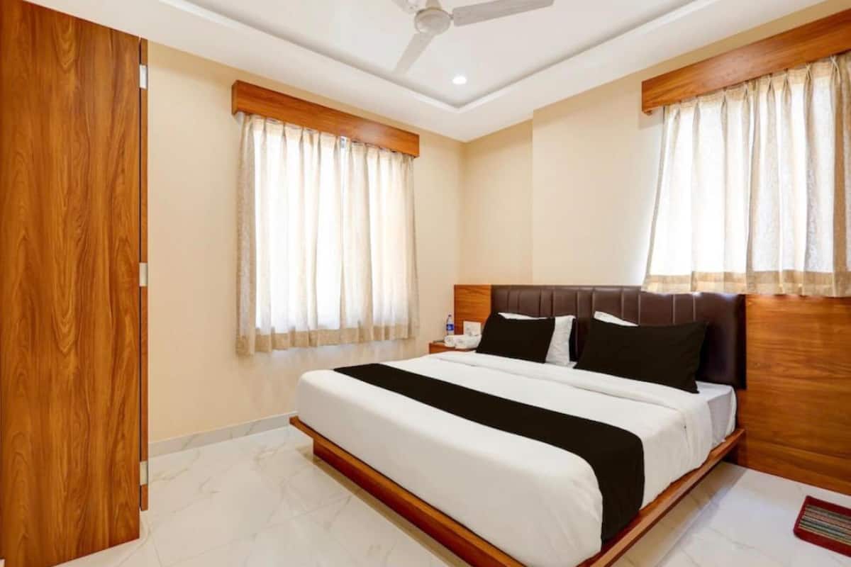 Quarto de hotel com cama grande, cabeceira de madeira, cortinas brancas e ventilador de teto.