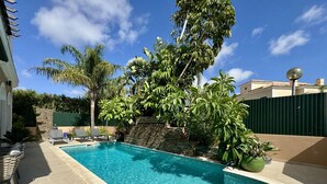 Piscina com muro de pedra e palmeiras, cercada por um espaço de pátio com azulejos.