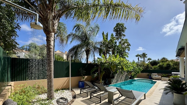 Piscina com espreguiçadeiras, uma estátua e cerca verde.