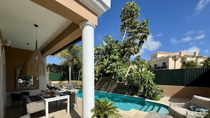 Área de estar externa com piscina, móveis de vime e uma mesa de jantar.