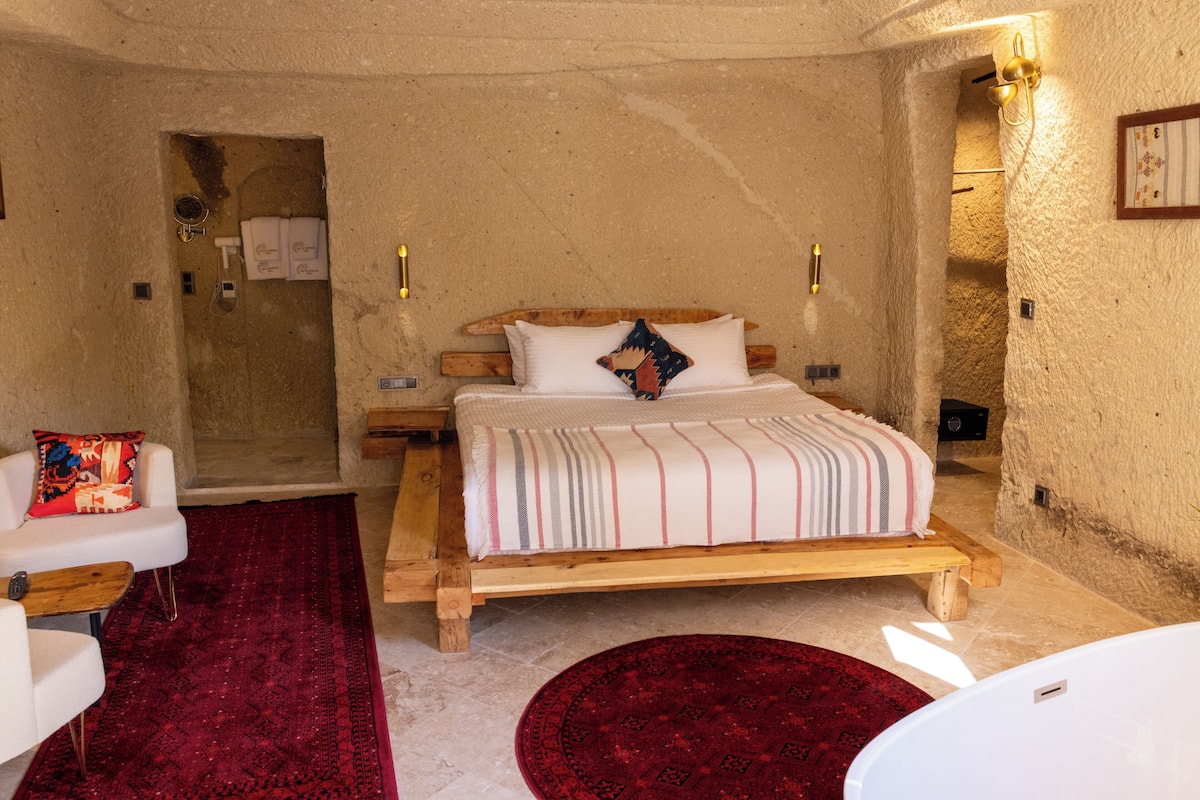 Um quarto com uma cama, um tapete vermelho, uma cadeira branca e uma mesinha de cabeceira de madeira.