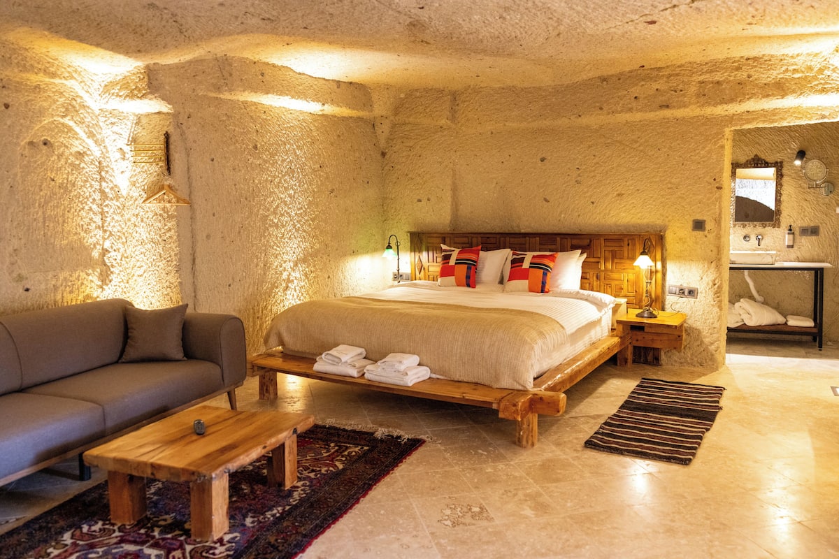 Quarto com cama, sofá, mesa de madeira e banheiro com pia e espelho.