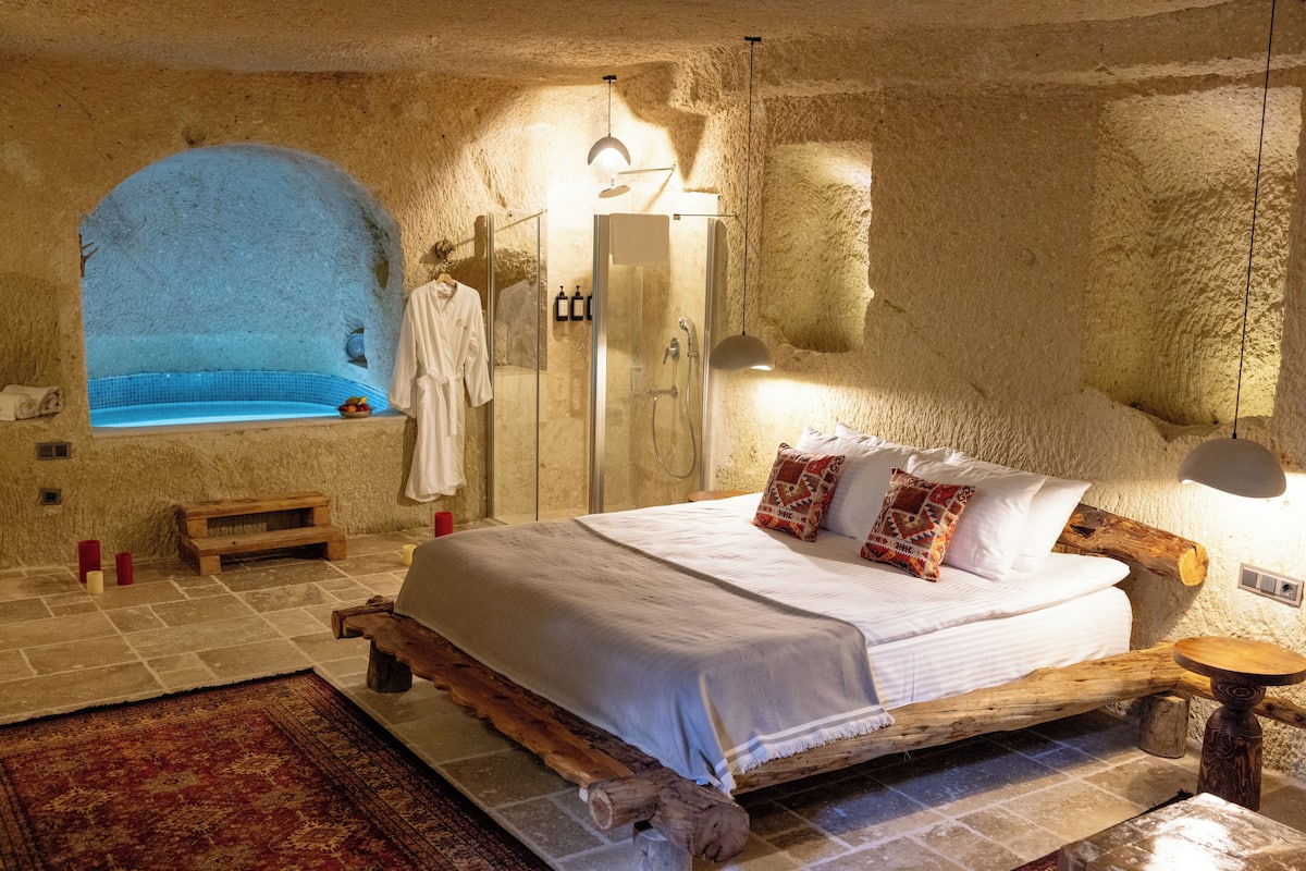 Quarto com uma cama grande, cabeceira de madeira, banheira embutida e chuveiro de canto.