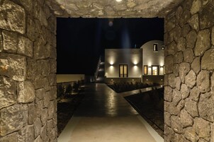 Arcada de pedra que dá acesso a um edifício moderno com escadaria e janelas iluminadas.