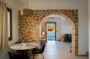 Uma sala de jantar com um arco de pedra, uma mesa redonda com cadeiras e vista através de uma porta aberta.