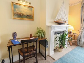 Quarto com uma mesa de jantar, uma cadeira, lareira com manto branco, quadro emoldurado, um vaso e uma planta em vaso.