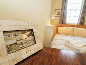 Quarto de hotel com uma fotografia histórica emoldurada, cabeceira de madeira, luminária de cabeceira e janela com cortinas.