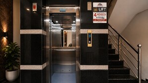 Um elevador com visor digital, placa indicando capacidade máxima de 4 adultos com bagagem e aviso de segurança.
