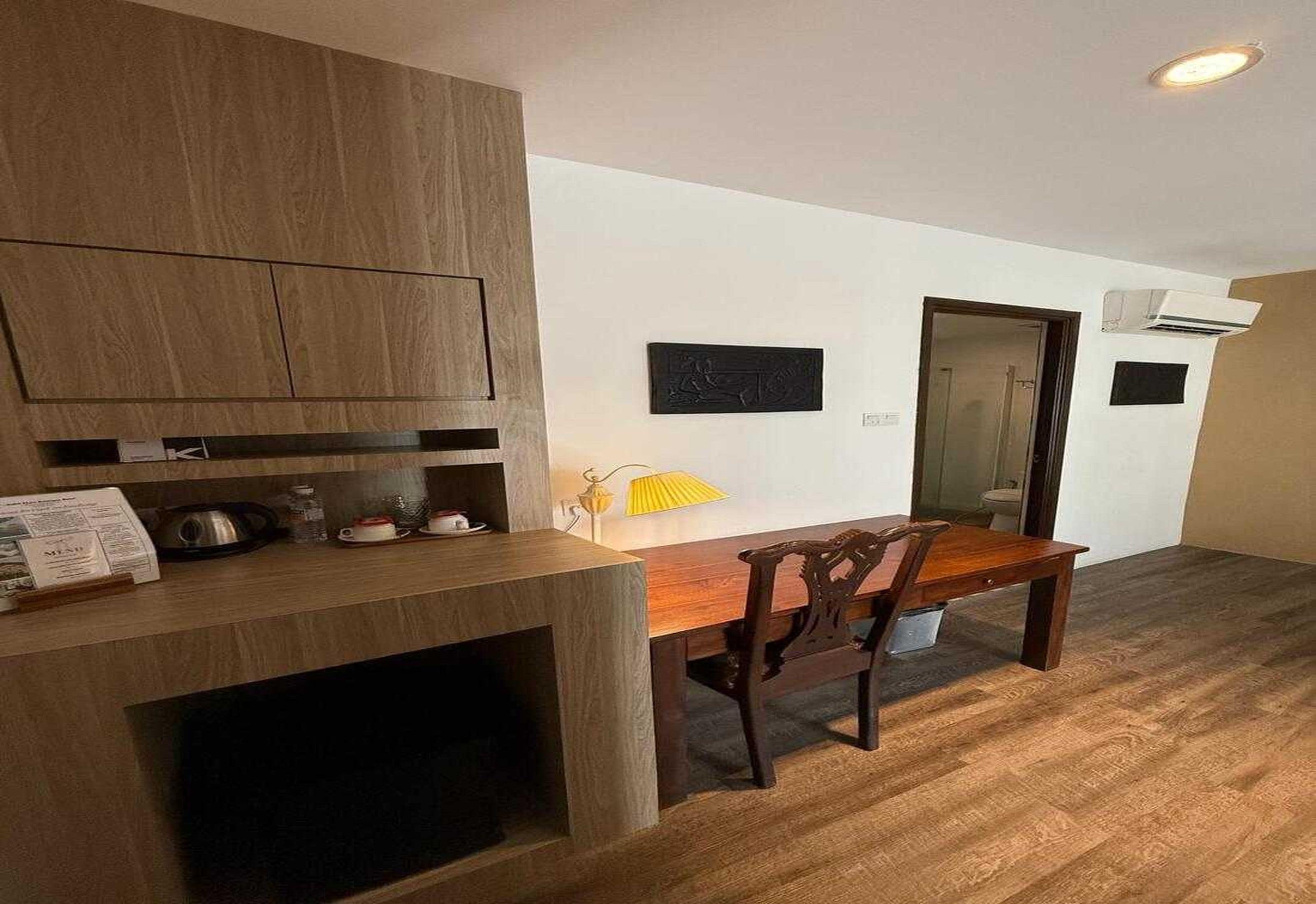 Cozinha compacta com armários de madeira, uma mesa de jantar com cadeiras e uma pequena luminária amarela.