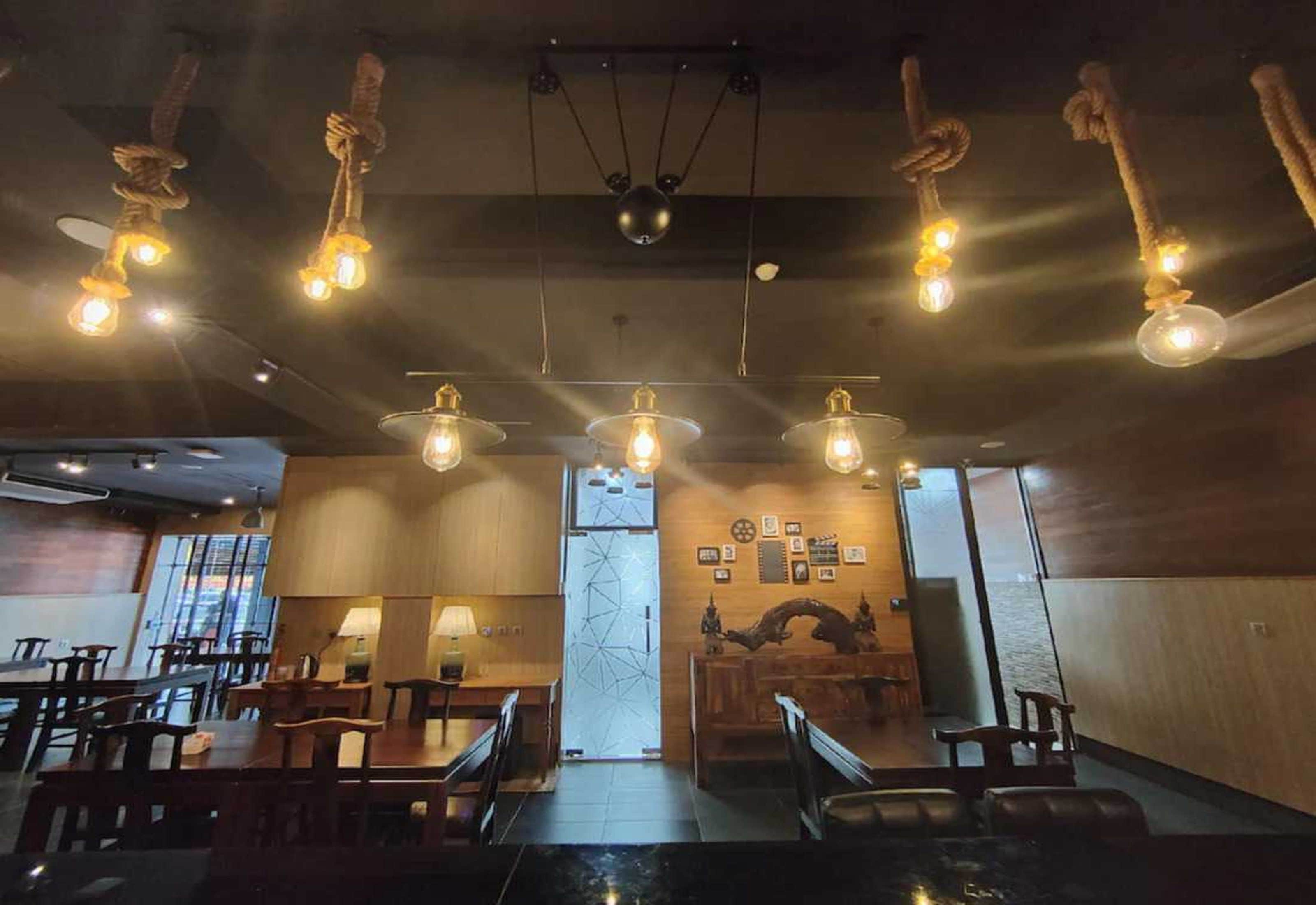 Interior de restaurante com luminárias pendentes, mesas e cadeiras de madeira.