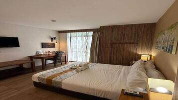 Quarto de hotel com cama grande, escrivaninha, cadeira, televisão na parede e janela com cortinas.