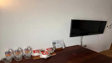 Mesa de madeira com televisão de tela plana na parede, jornal e bandeja com xícaras e temperos.