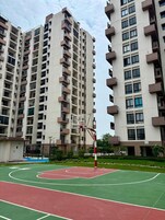 Um edifício residencial com vários andares, varandas, quadra de basquete e um pequeno jardim.