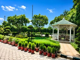 Um jardim com um gazebo, plantas em vasos e um céu azul límpido.