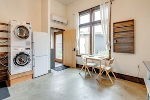 Uma lavanderia com máquina de lavar e secadora, uma pequena mesa com cadeiras e uma janela com cortinas.