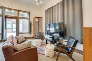 Sala de estar com sofá, pufe, televisão e poltronas.