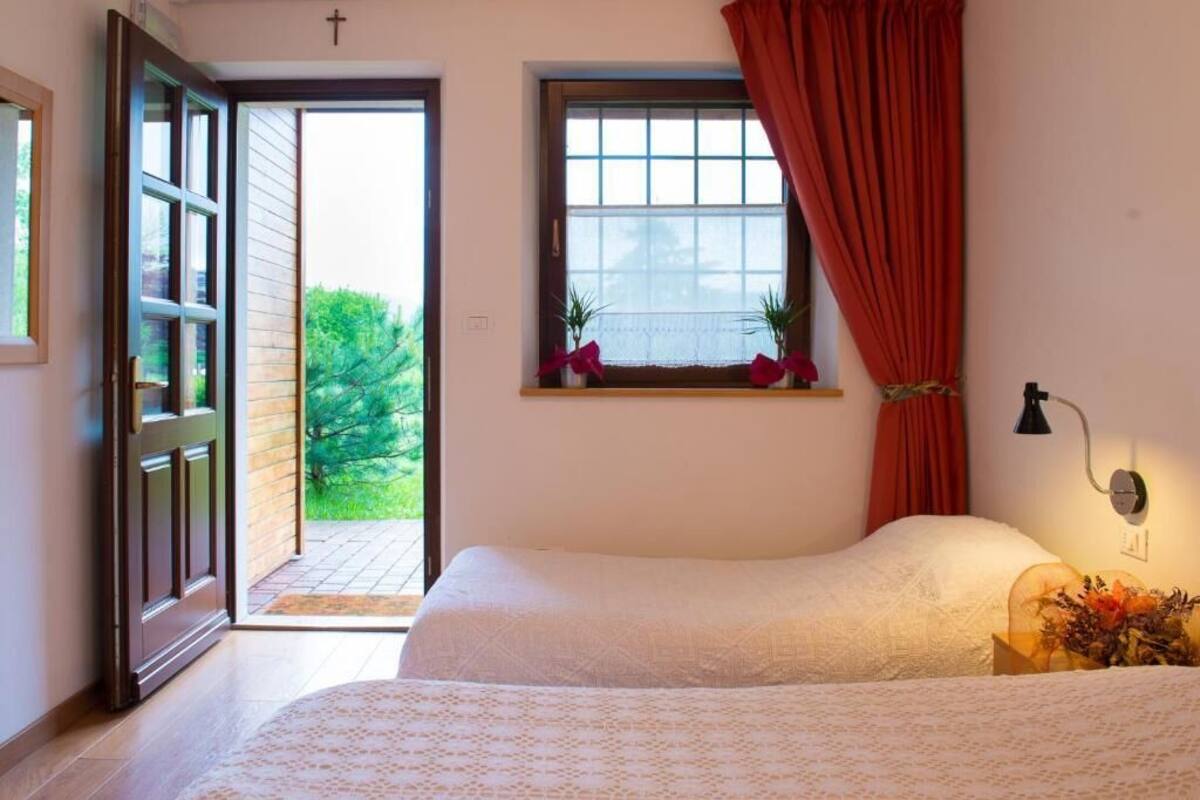 Quarto com cama, janela com vista, porta e luminária fixada na parede.