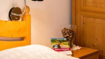 Quarto com cabeceira de madeira, uma escrivaninha com luminária, um livro e um recipiente de vidro.