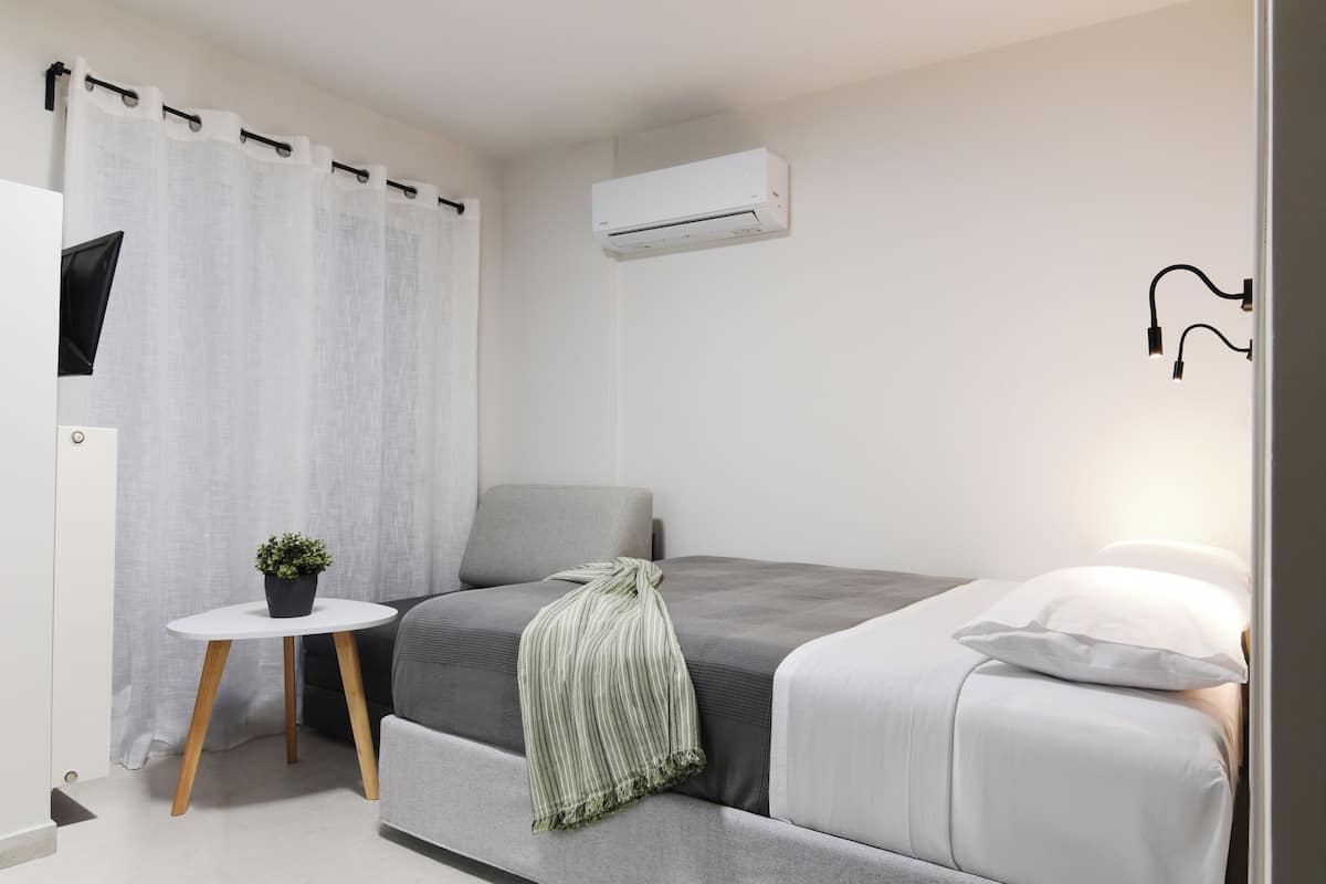 Quarto moderno com cama, mesa de cabeceira, aparelho de ar condicionado e uma pequena planta em vaso.