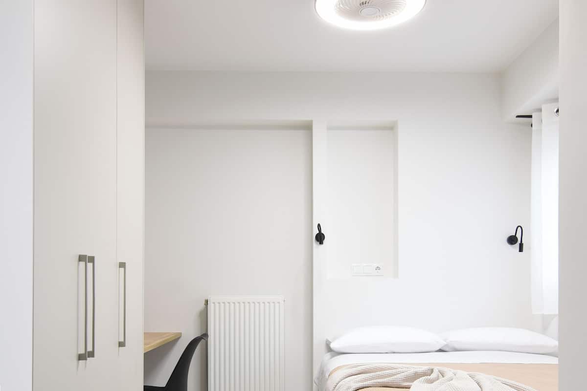Quarto moderno com cama, mesa de cabeceira, cadeira e radiador.
