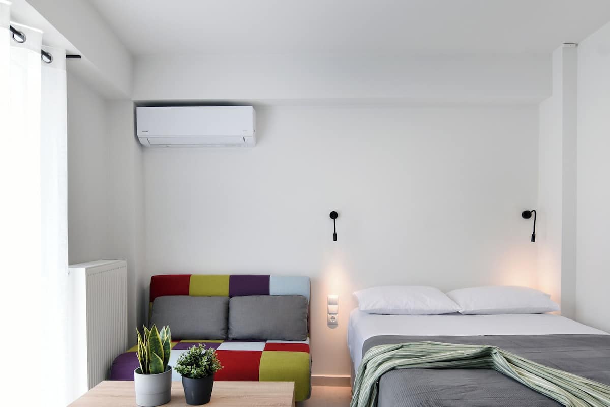Quarto moderno com cama, mesas de cabeceira, sofá colorido e luminária no teto.