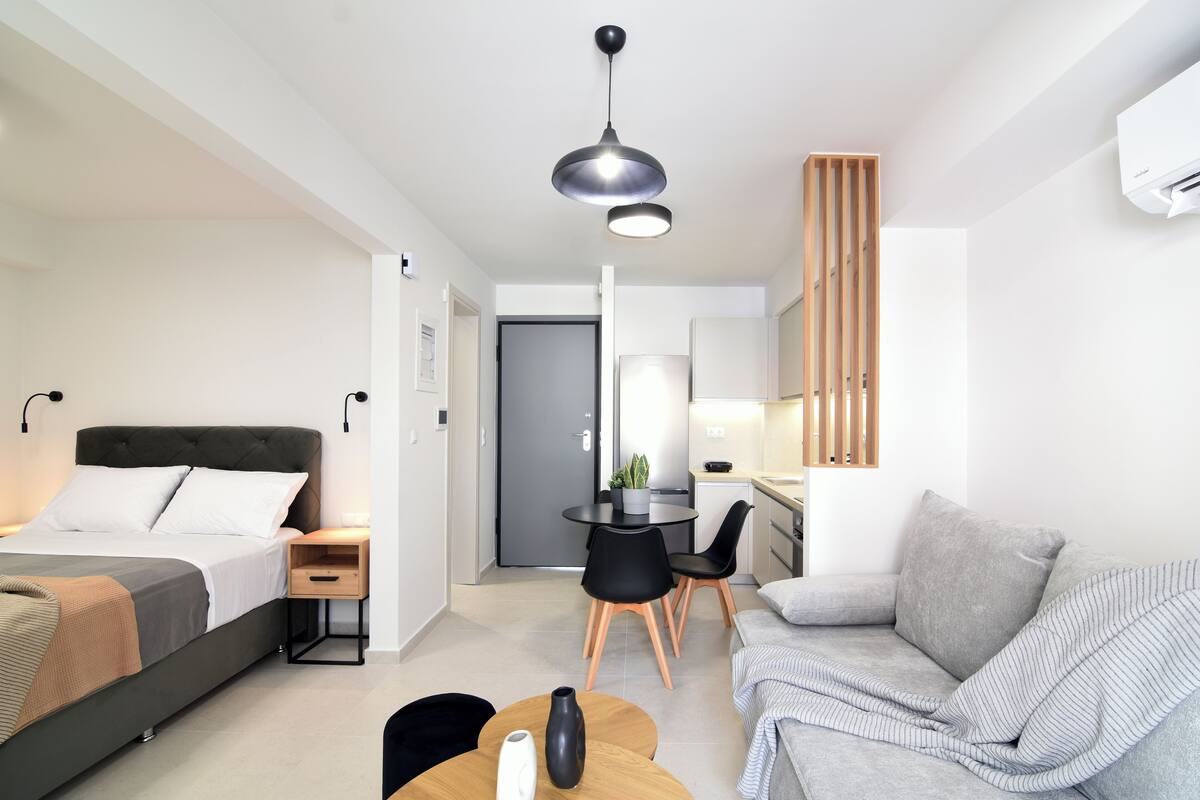 Quarto de hotel moderno com cama, sofá, mesa de jantar e cozinha.