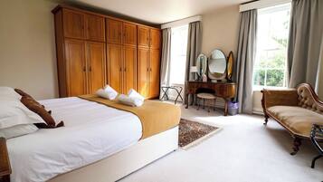 Quarto de hotel com cama grande, guarda-roupa de madeira, secretária com espelho e janela com cortinas.