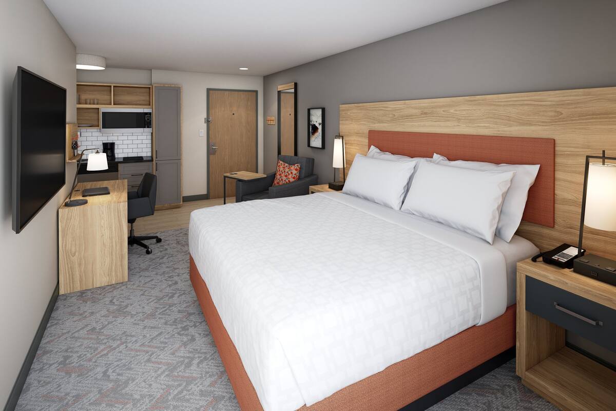 Quarto de hotel com cama, escrivaninha, cadeira, televisão, micro-ondas e porta para o banheiro.