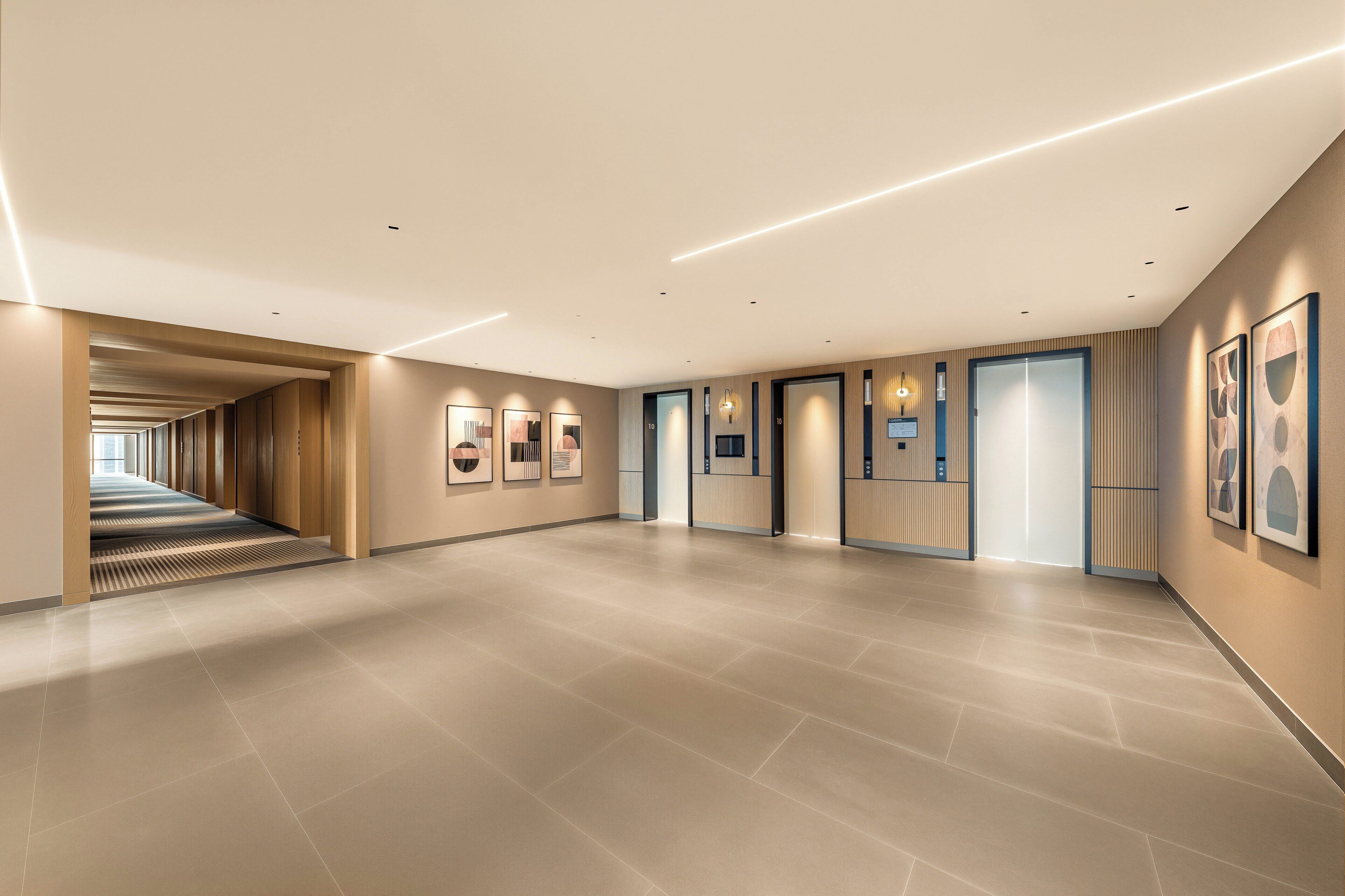 Um corredor espaçoso e moderno, com cores neutras, iluminação embutida e obras de arte emolduradas nas paredes.