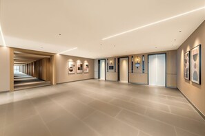 Um corredor espaçoso e moderno, com cores neutras, iluminação embutida e obras de arte emolduradas nas paredes.